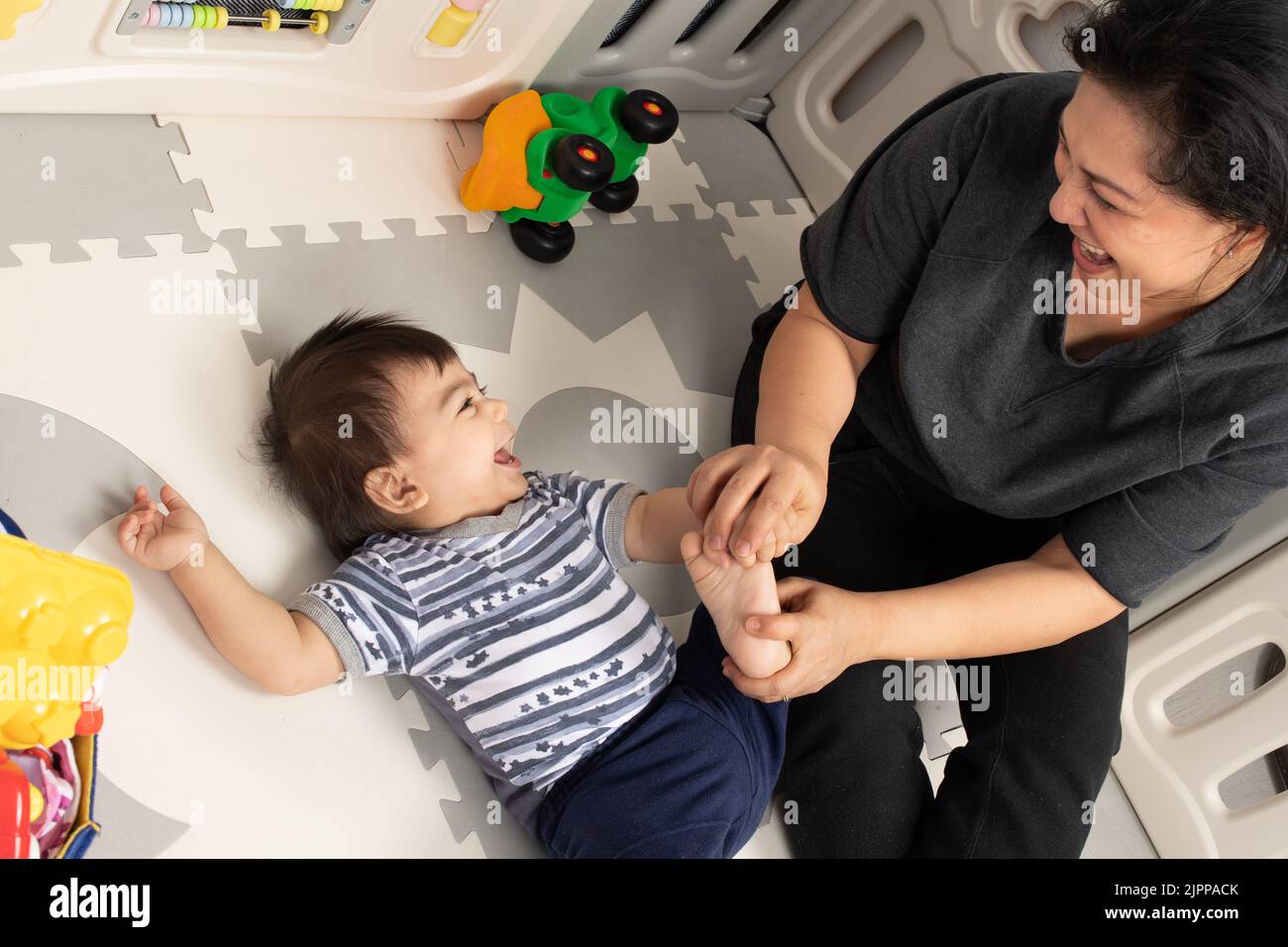 11 month old baby boy at home playful interaction with mother, laughing as she tickles his foot ...