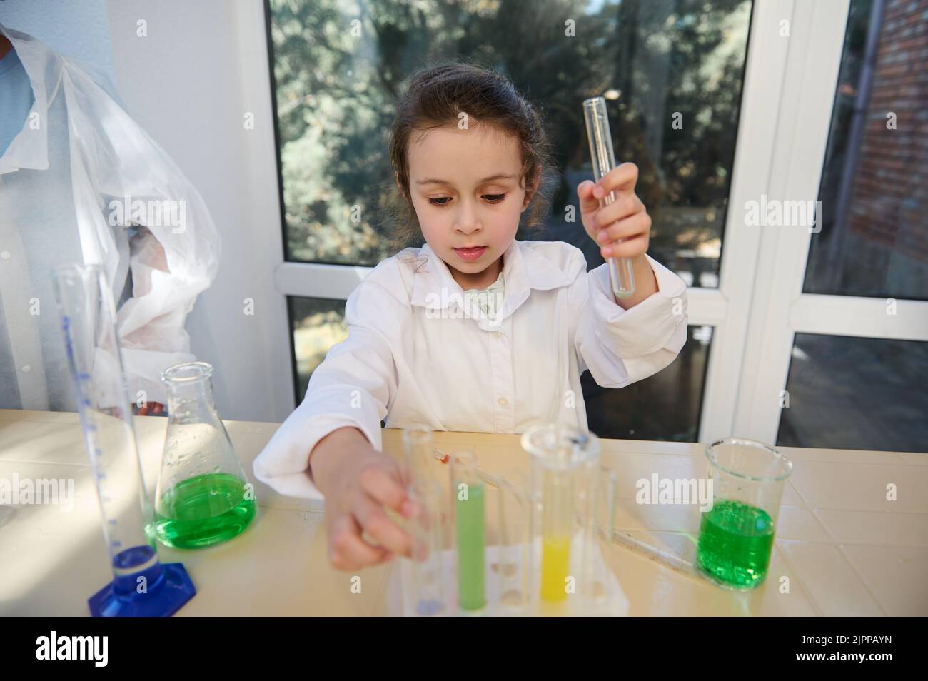Happy, inspired Caucasian preschooler girl pours and combines chemicals ...