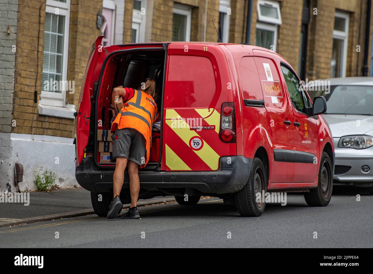 female post office worker getting letters and parcels from the back of a red royal mail van on a ...