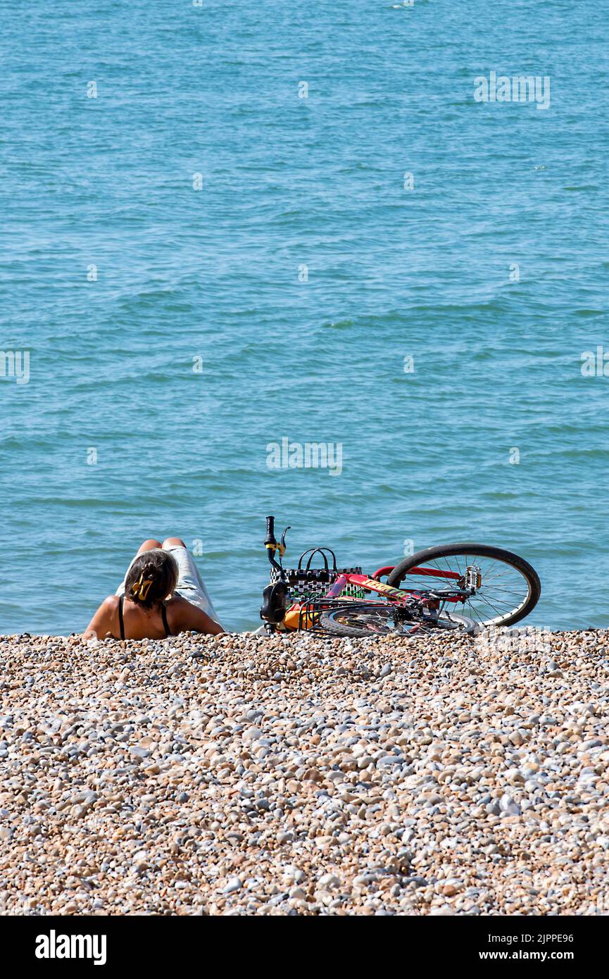 lady lying on a stony pebble beach on the shingle next to her bicycle ...