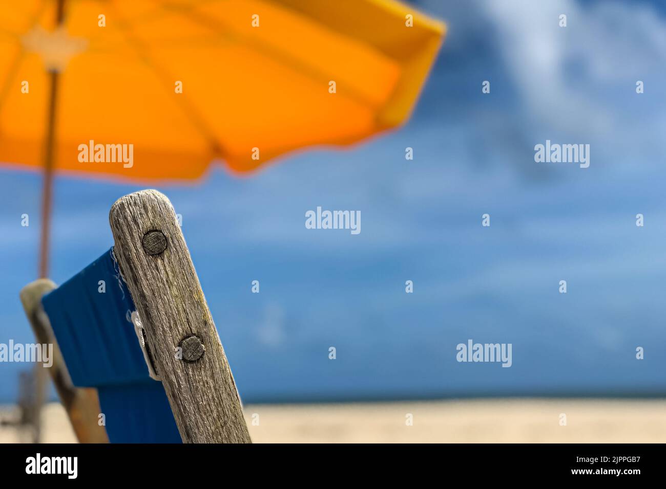 Closeup of wooden deck chair and yellow beach umbrella convey a ...