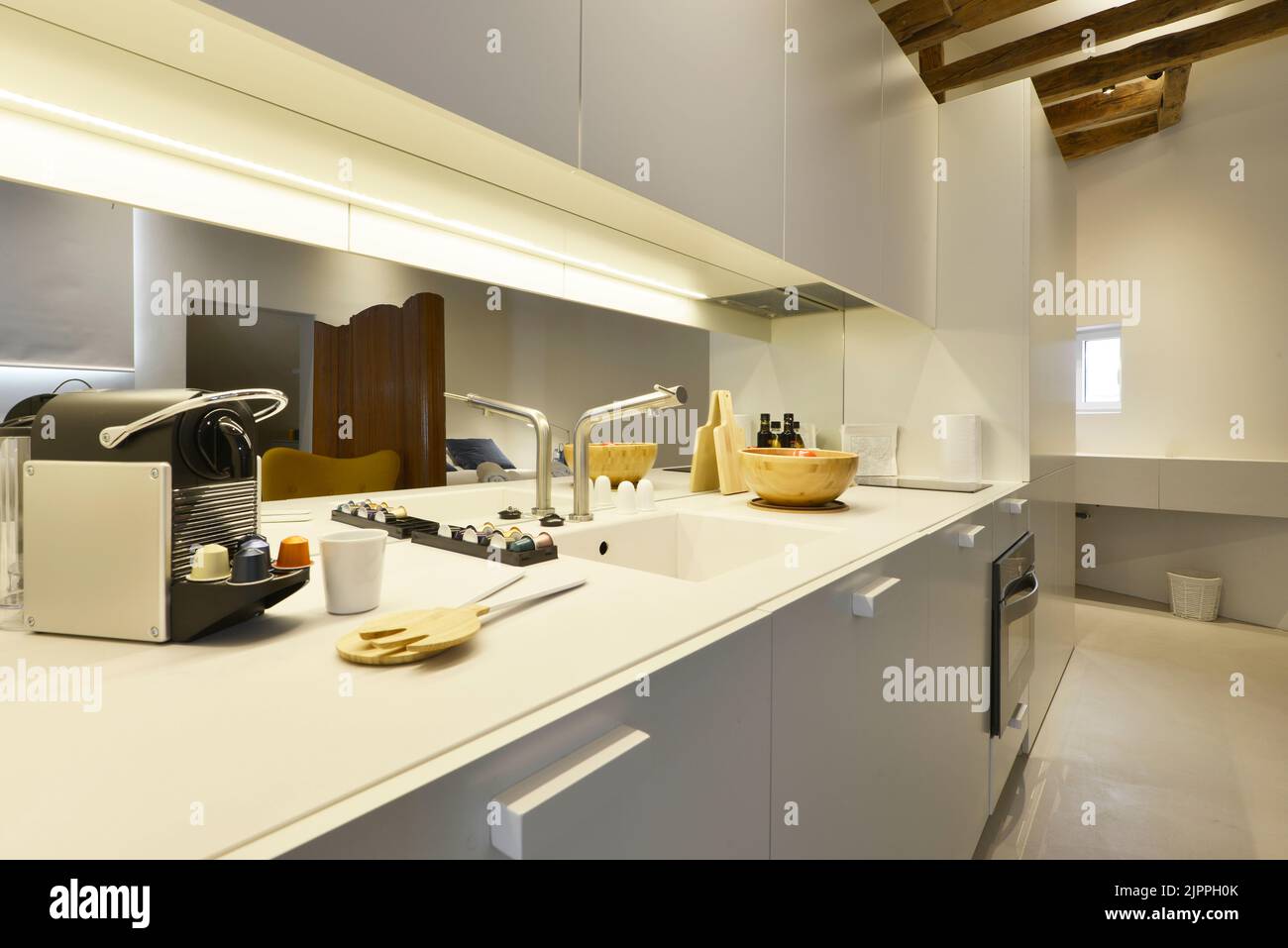 Kitchen with white wooden cabinets, mirrors on the wall, coffee capsule ...