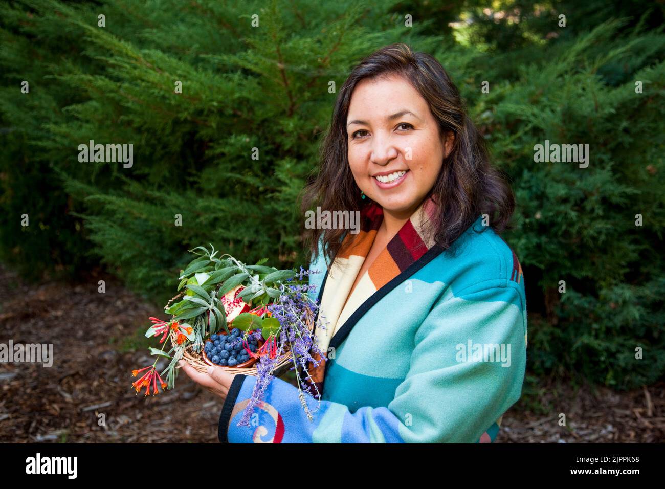 First Nations woman herbalist holds up a basket of natural plants and ...
