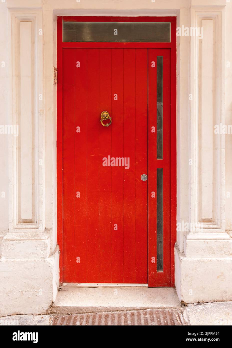 A vertical shot of a vintage red front door of a white building in ...