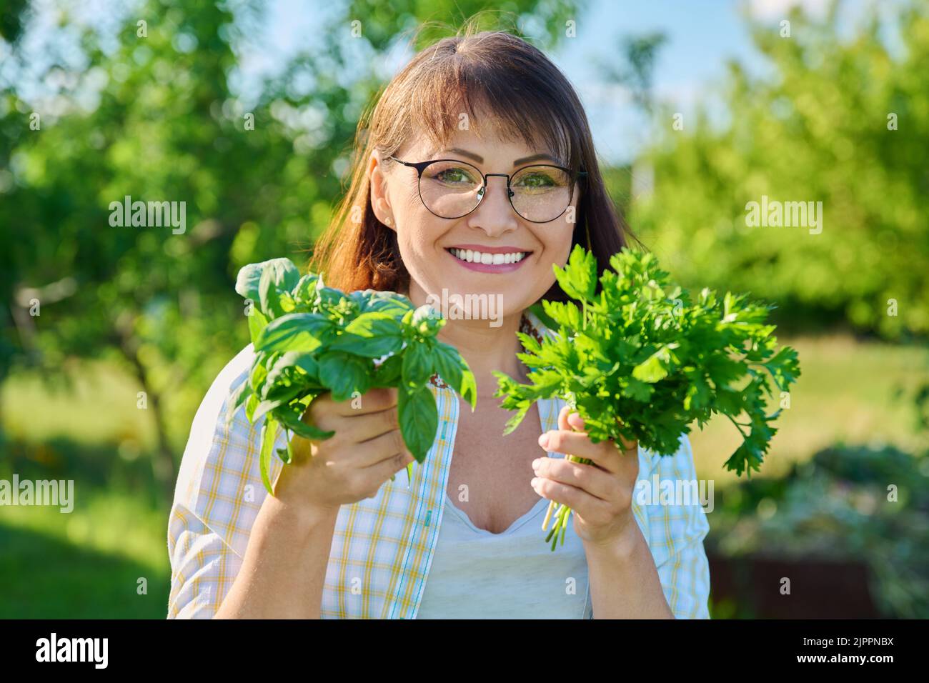 Happy woman with herb harvest bunch of parsley and basil in garden ...