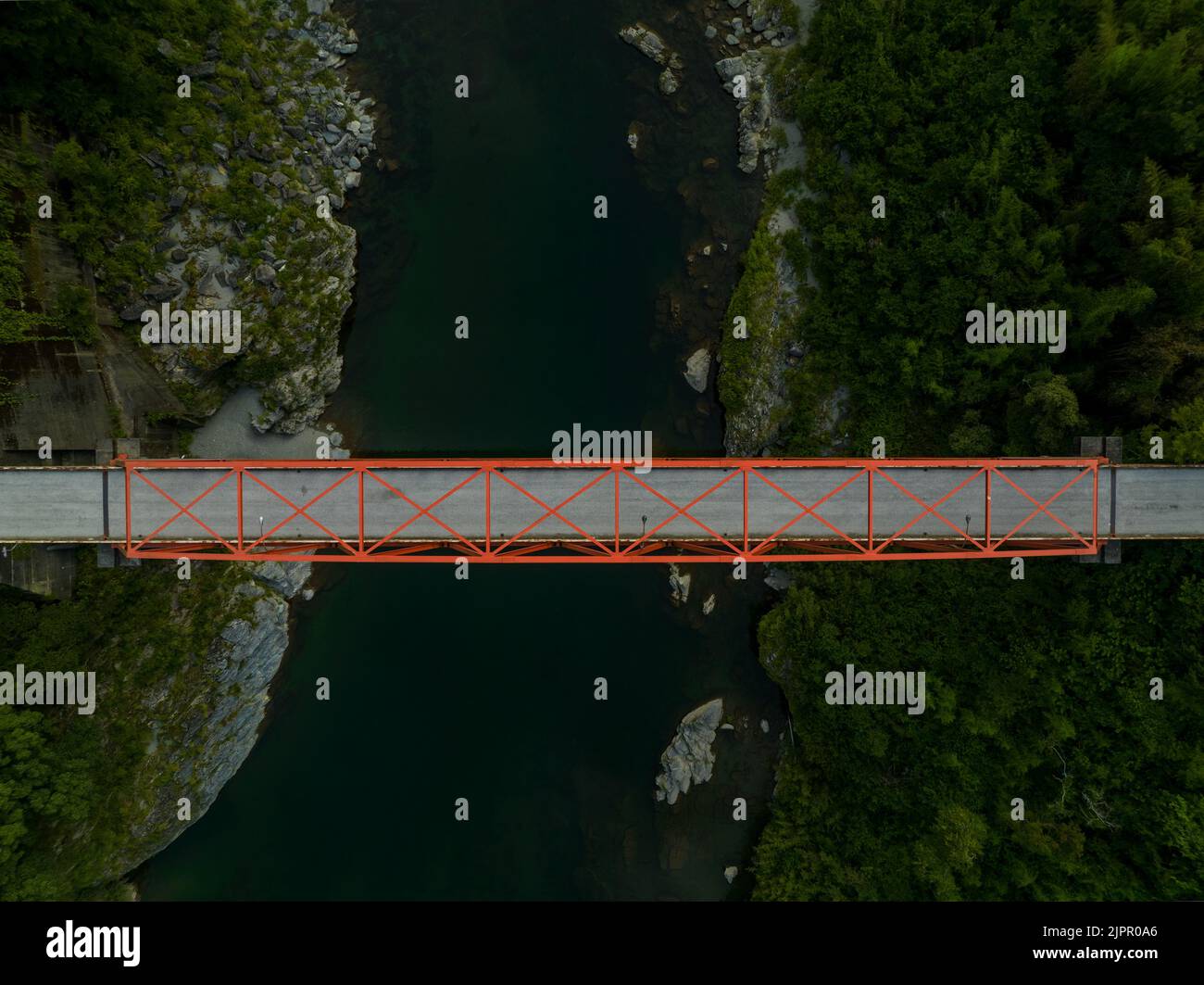 Overhead aerial view of empty red bridge over small river and rocky ...