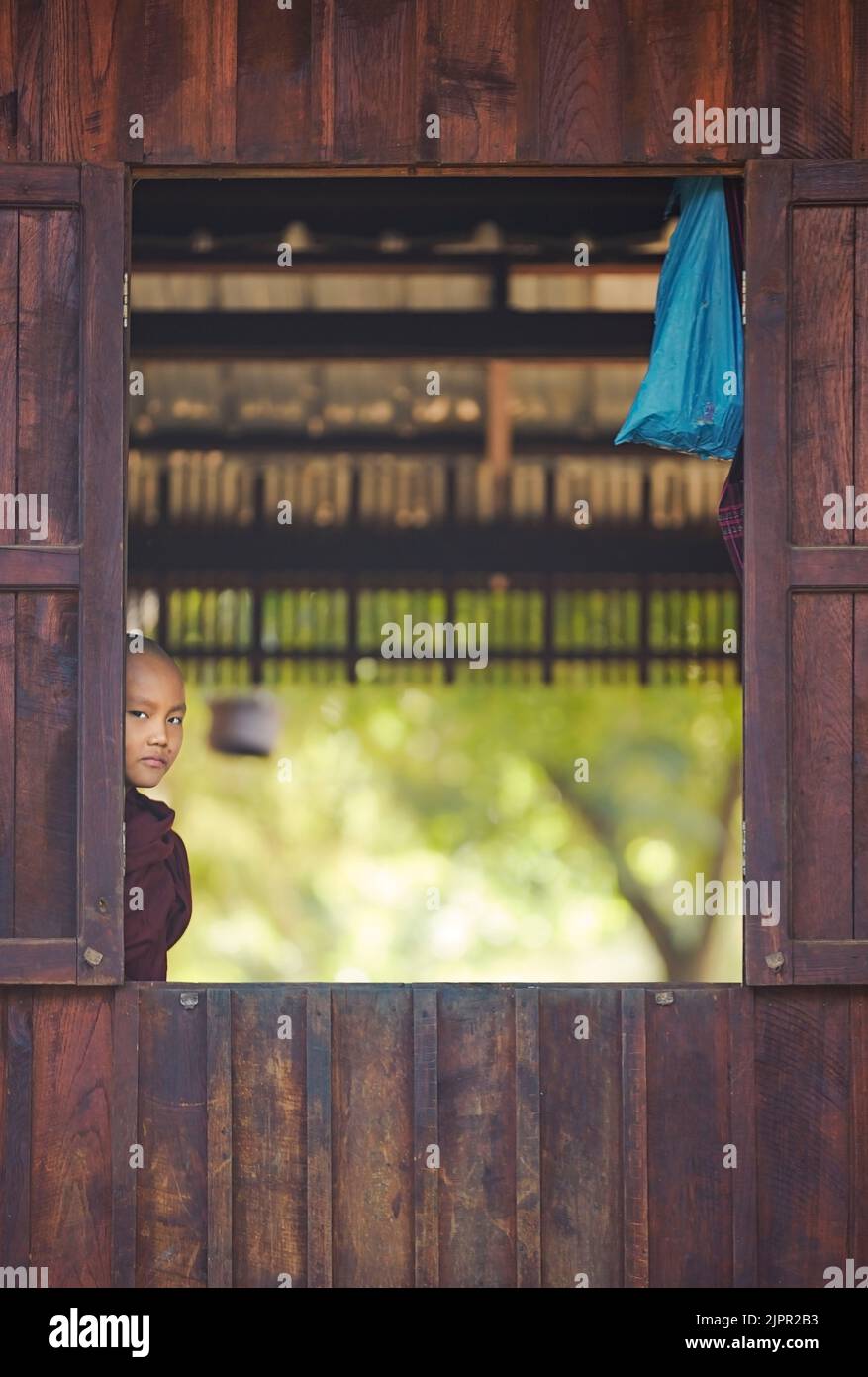 A novice monk at a wooden window of a Buddhist monastery in Nyaung U ...