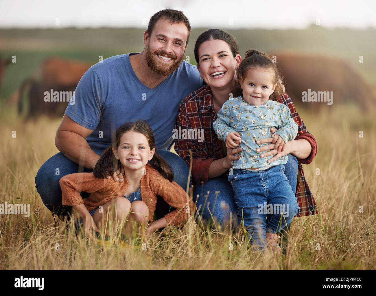 Portrait of happy family on a countryside farm field with cows in the ...