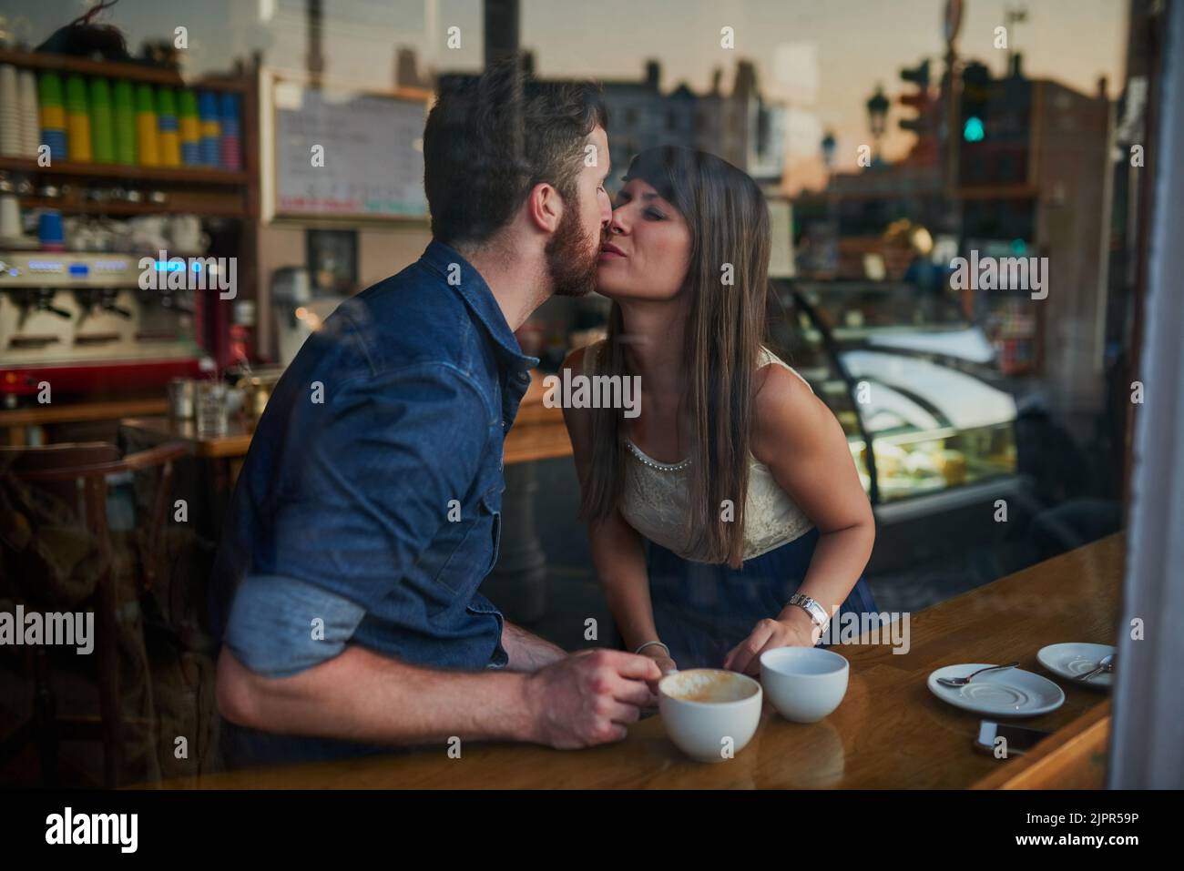 Its their first date. an affectionate young couple kissing while sitting in a coffee shop during ...