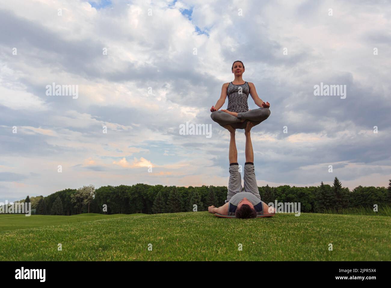 Young couple doing acro yoga in park. Man lying on grass and balancing ...