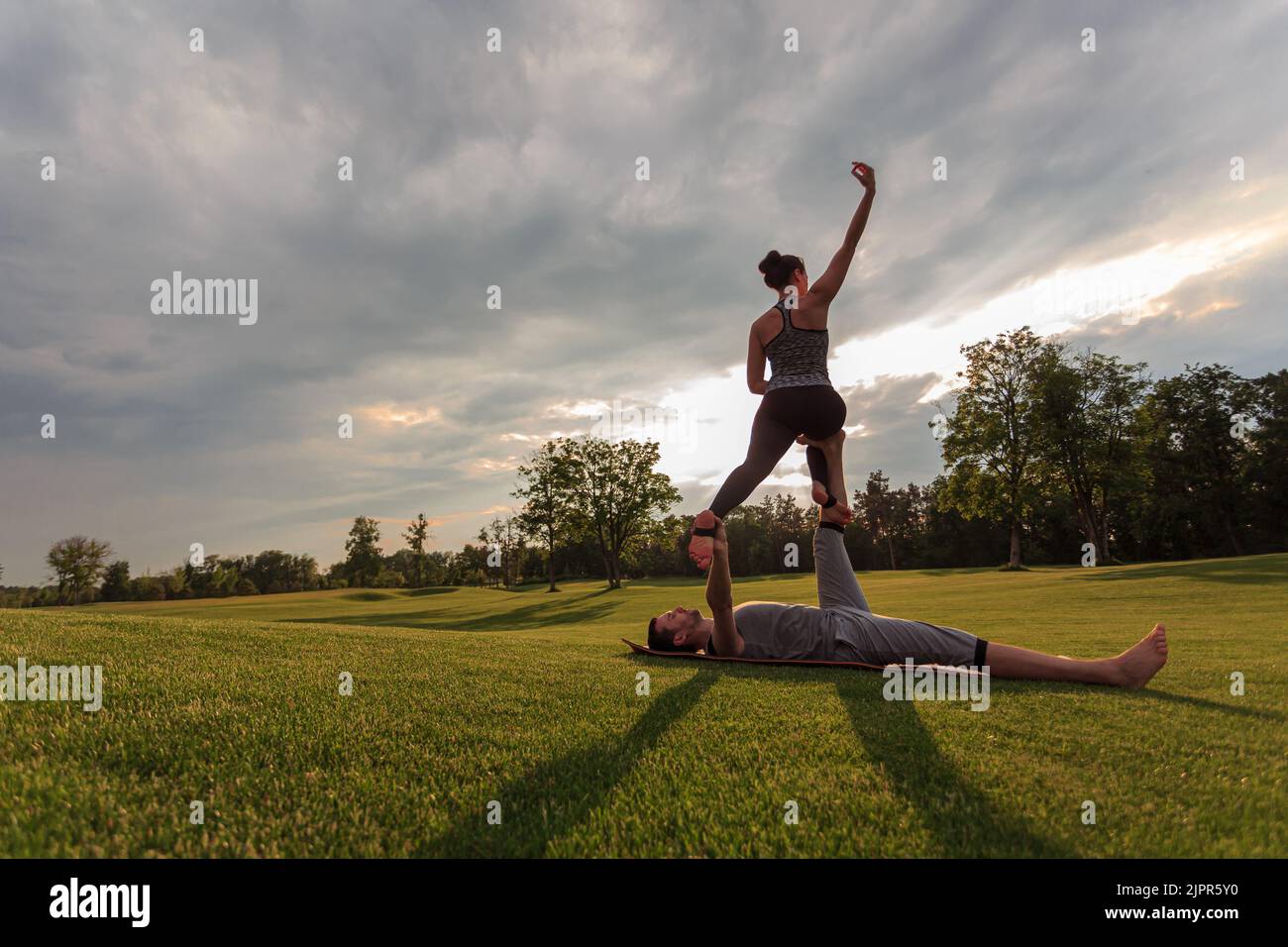 Healthy man lying on grass and balancing woman. Couple doing acrobatic ...