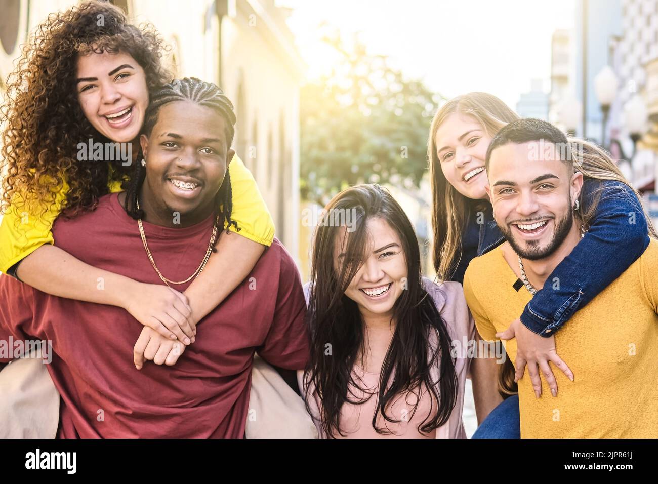 Multiracial young people walk happily in the city streets on piggyback ...