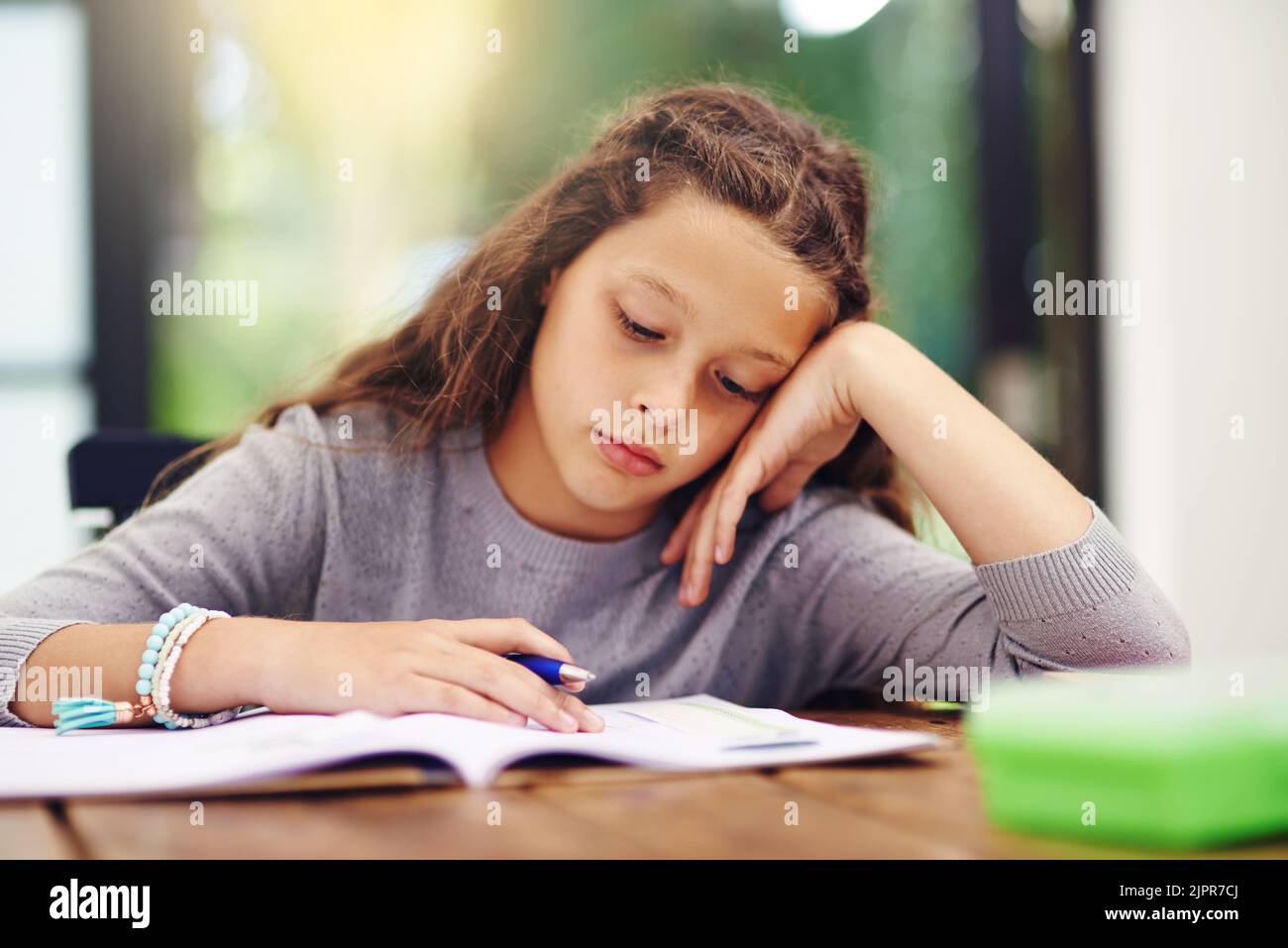 Trying to study but shed rather go play. a young girl doing homework ...
