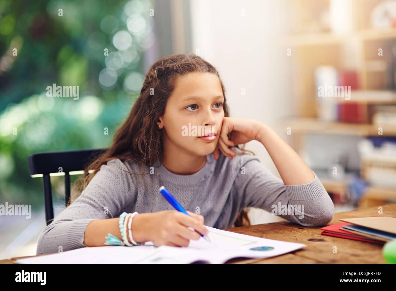 Thinking about the answer. a young girl doing homework inside Stock ...