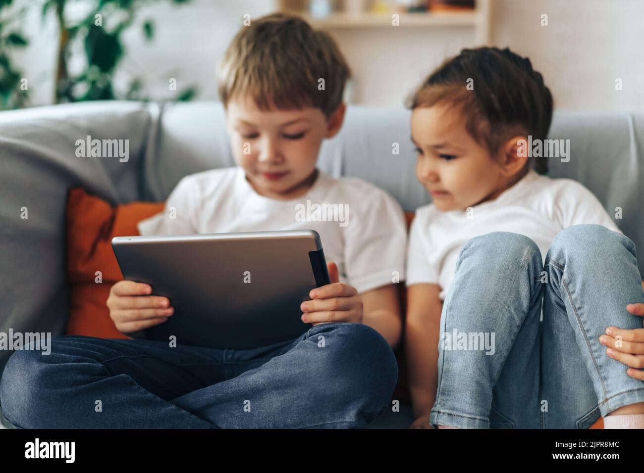 Children sitting on the couch watching videos on the tablet Stock Photo ...