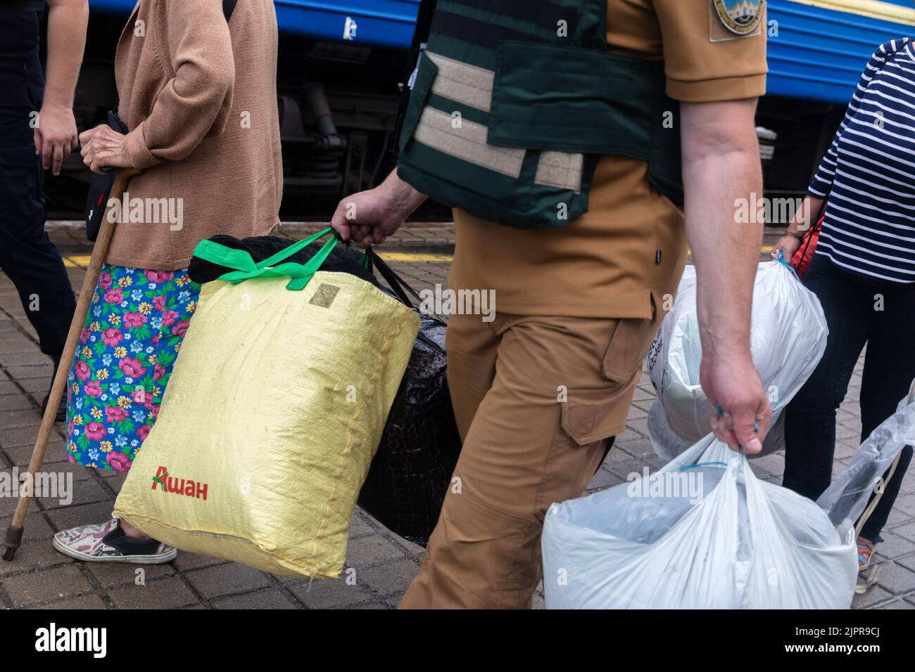 A man in a bulletproof vest helps the elderly carry their belongings ...