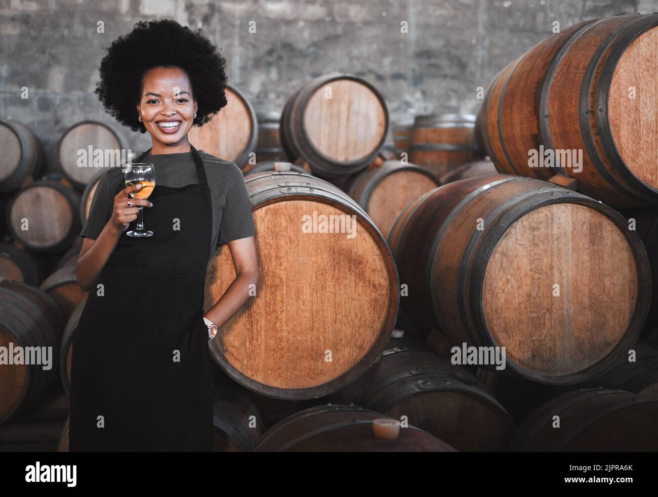 Portrait of a young woman winemaker standing with a glass with wooden ...