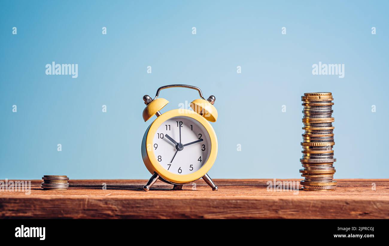 An alarm clock as a symbol of time and coins as a symbol of money. The ...