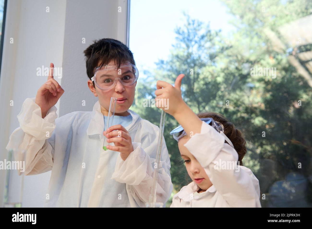Cheerful kids in white lab coat and safety goggles making experiments ...