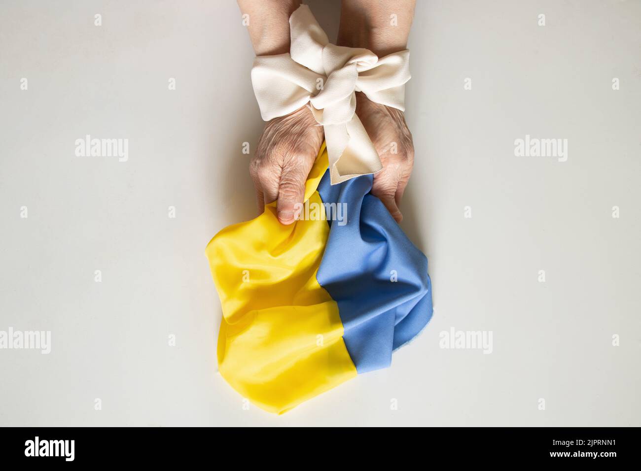 The hands of a Ukrainian woman tied with a white rope, with a yellow ...
