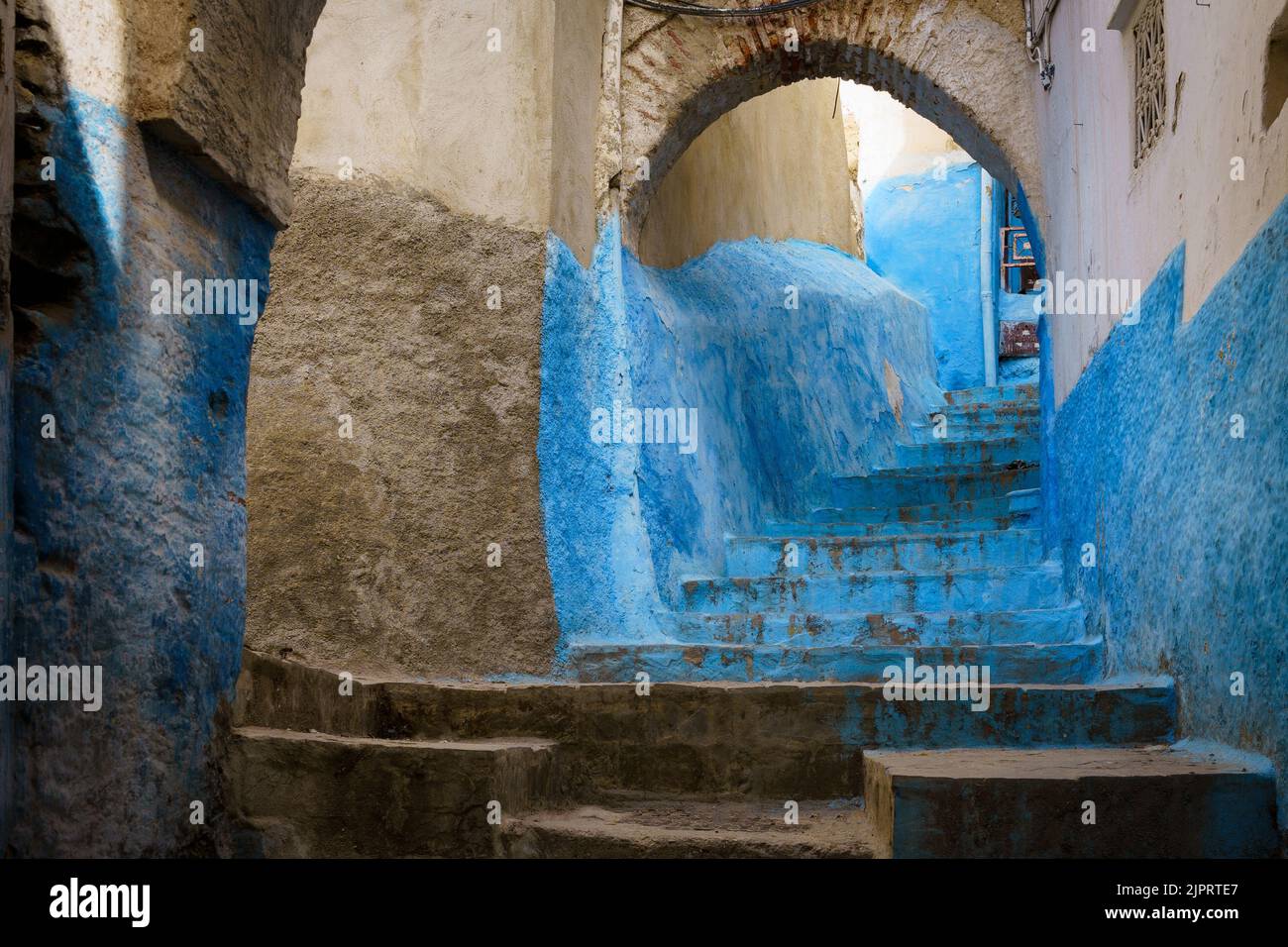 An arch gate with blue stairs on a medieval alley with plant pots in ...