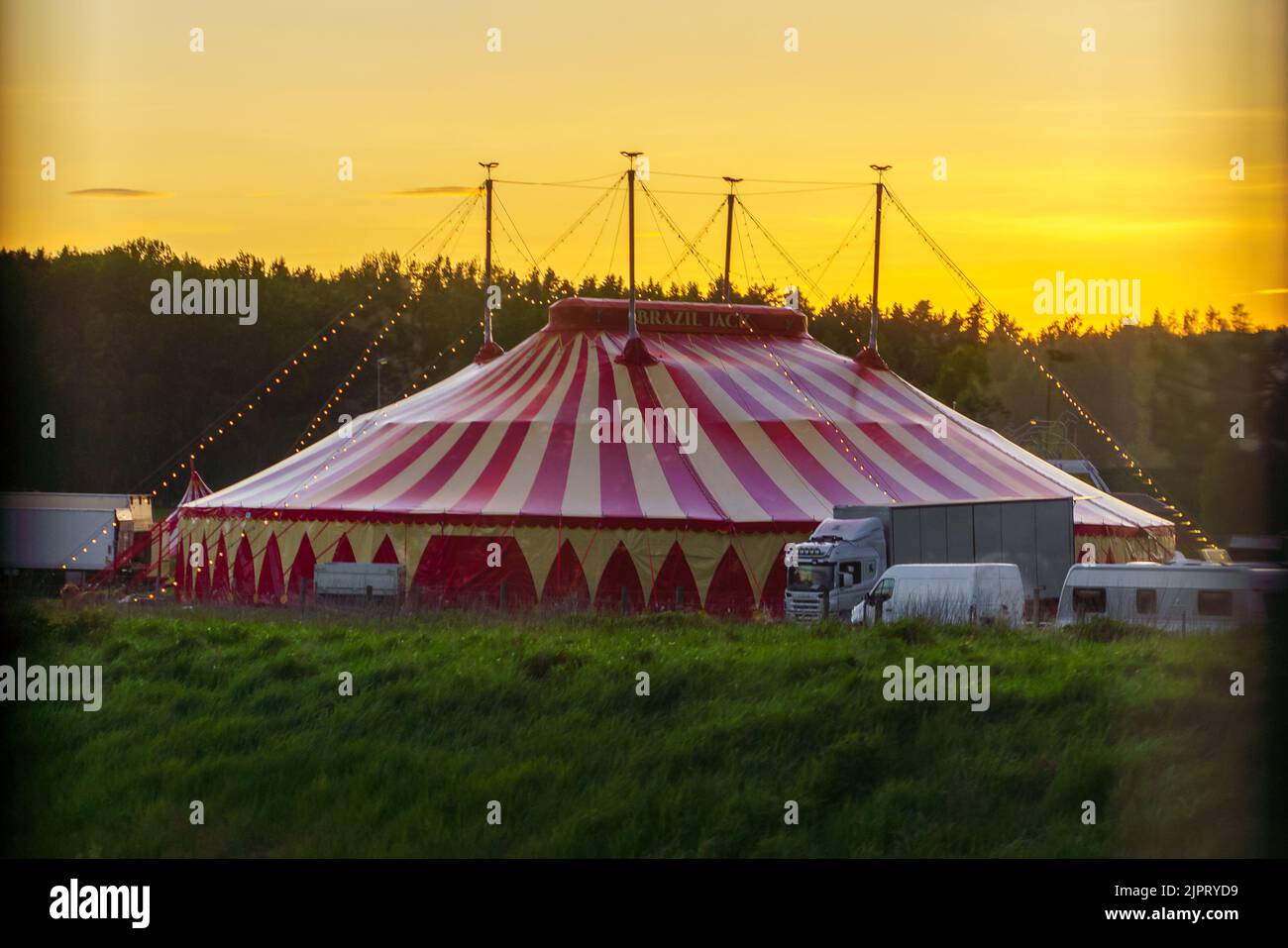 The striped circus tent on top of the green hill before the woods at ...