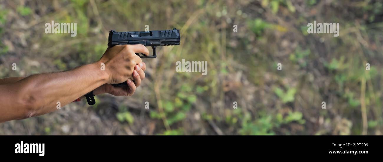Side view of arms stretched out aiming handgun. Gun training at outdoor ...