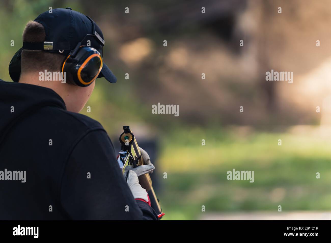 Rear view of man in black hoodie and cap wearing safety headphones ...
