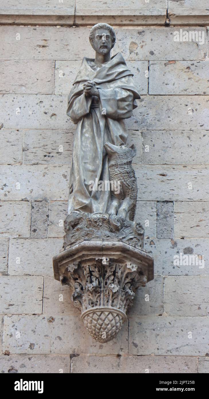 The vertical view of a marble statue of a monk standing with a dog on ...