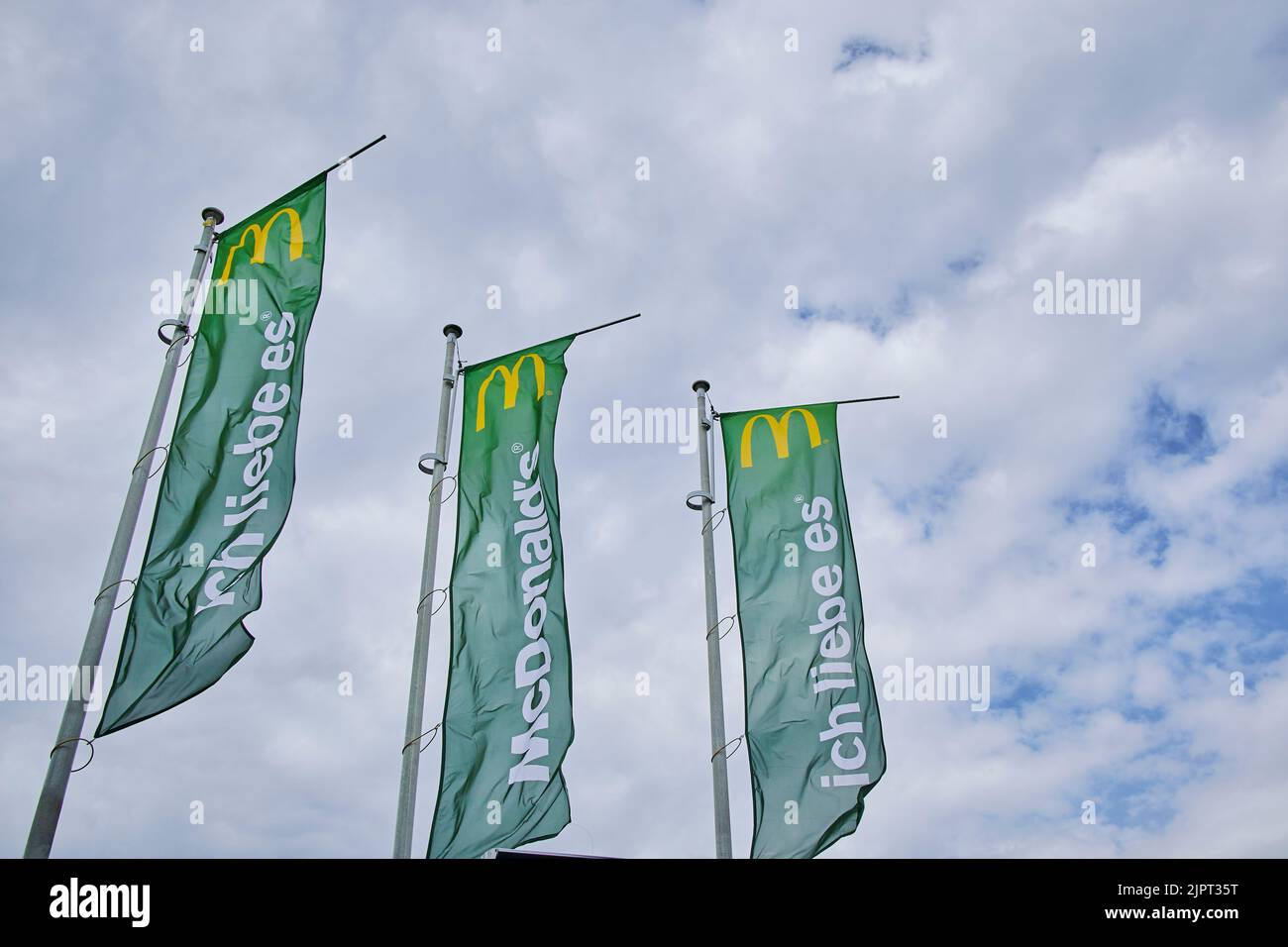 A low-angle shot of three green flags from a fast food restaurant under ...