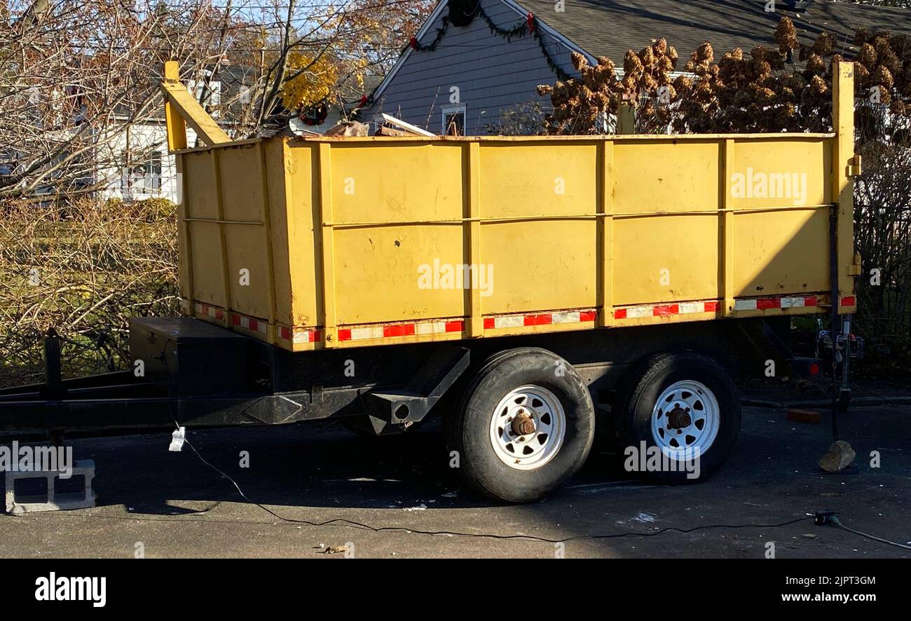 Side view of a large yellow dupmster on a trailer in a residential ...