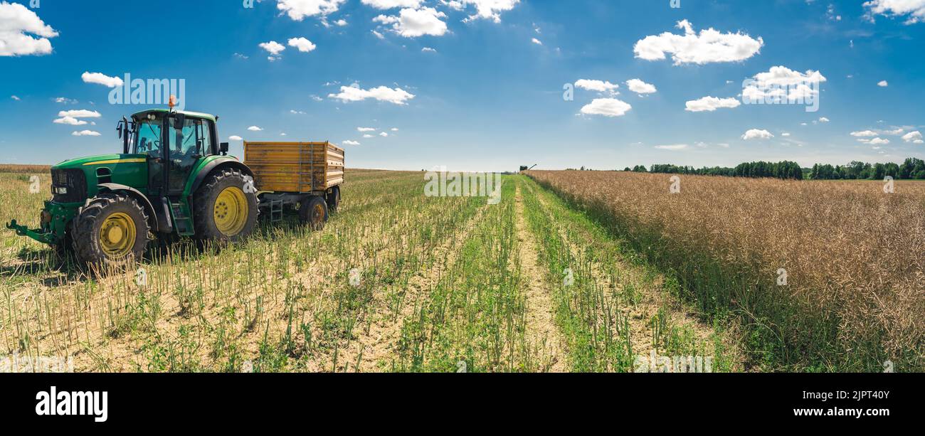 Wide panoramic shot of green tractor and a trailer on the left and ...