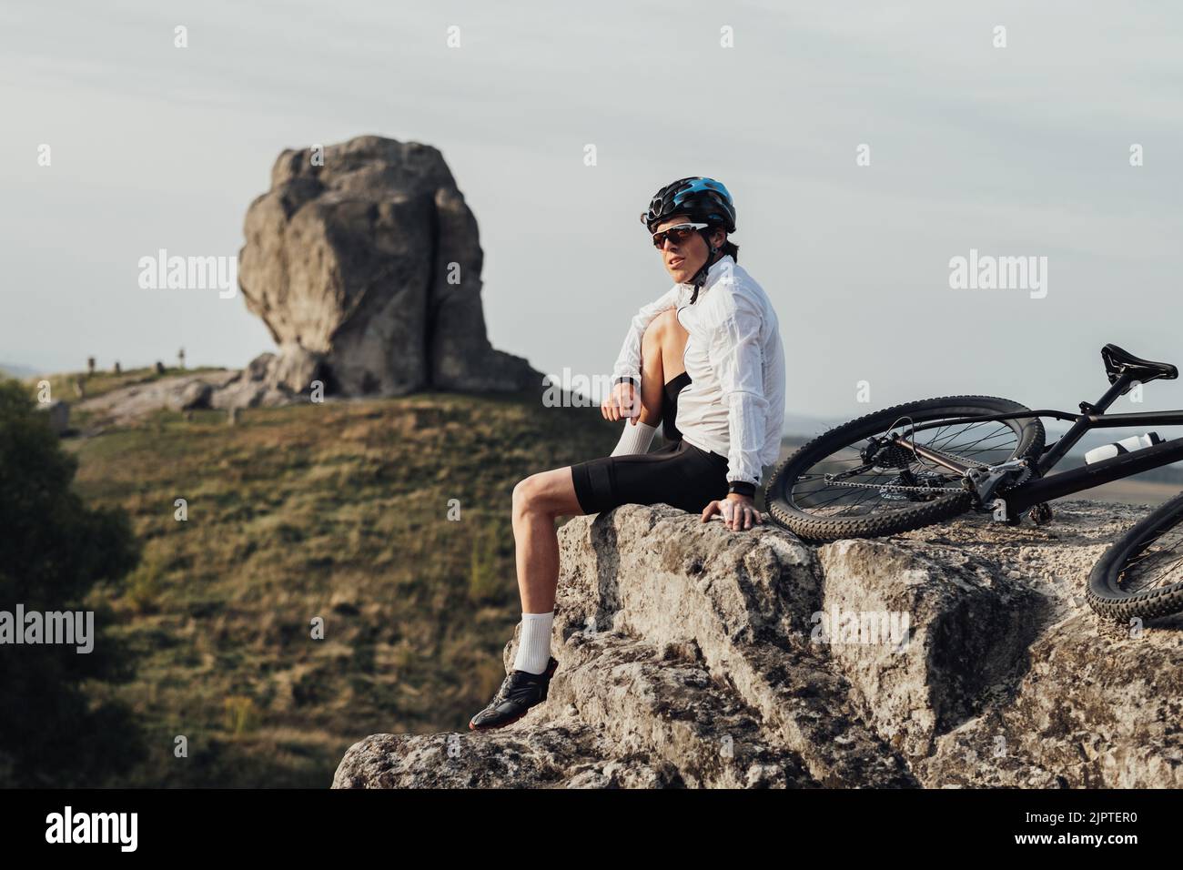 Equipped Professional Male Cyclist Sitting with Mountain Bike on Edge of the Rock and Enjoys ...