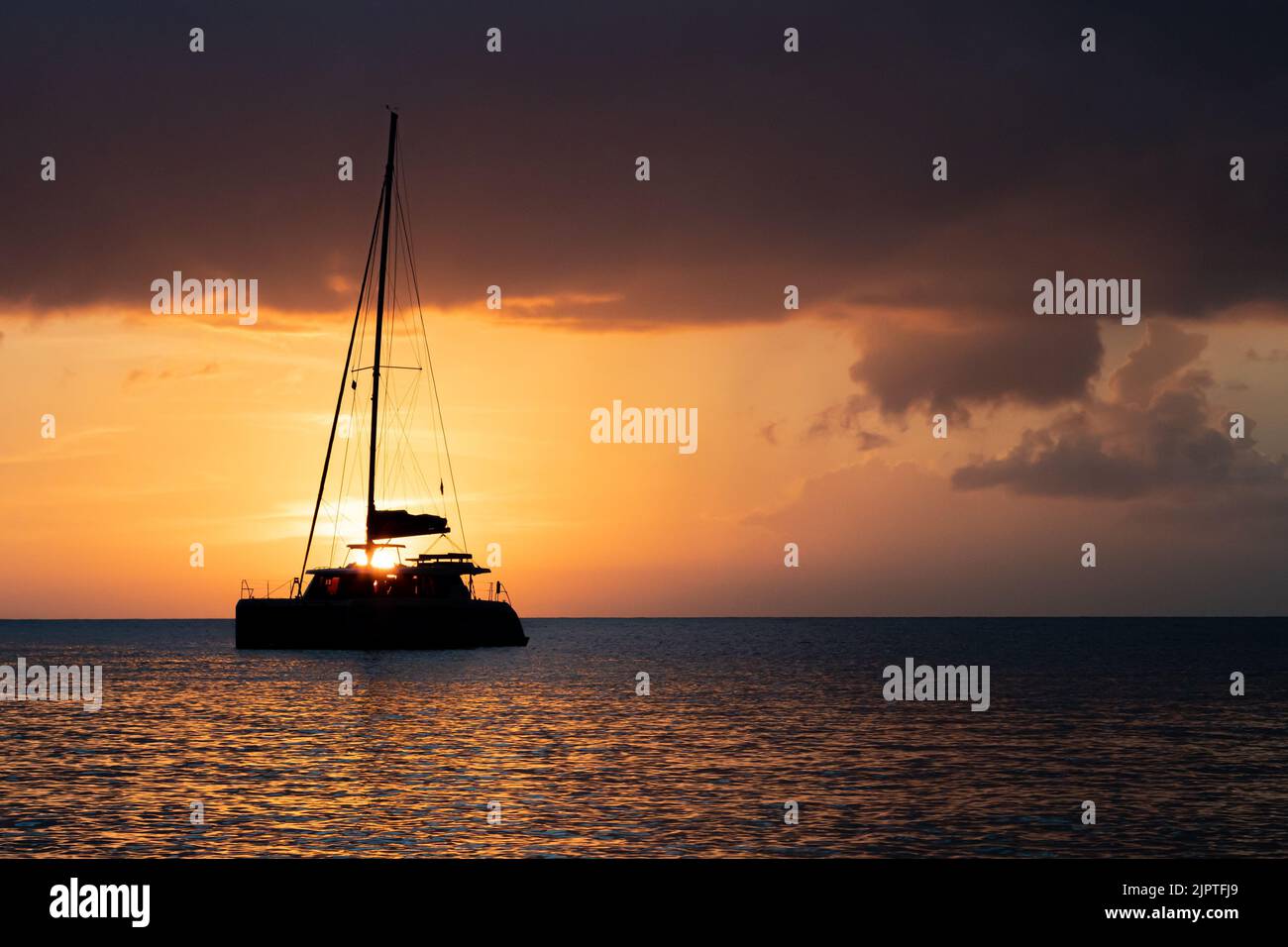 Silhouette of a sail boat sailing off into the light of sunset on the ...