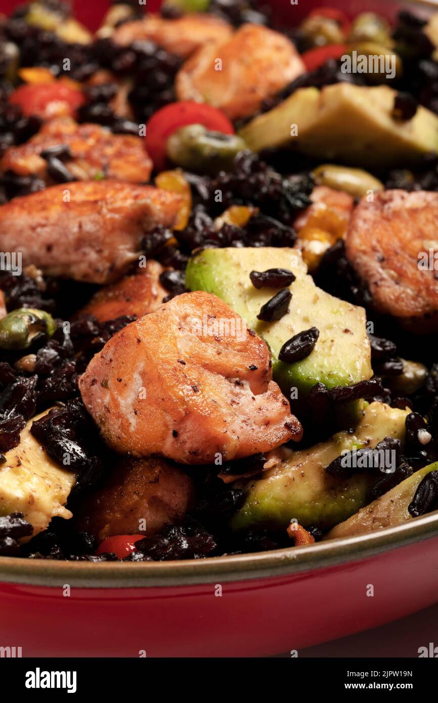 A red bowl of black rice with baked salmon, avocado, tomatoes, chili ...