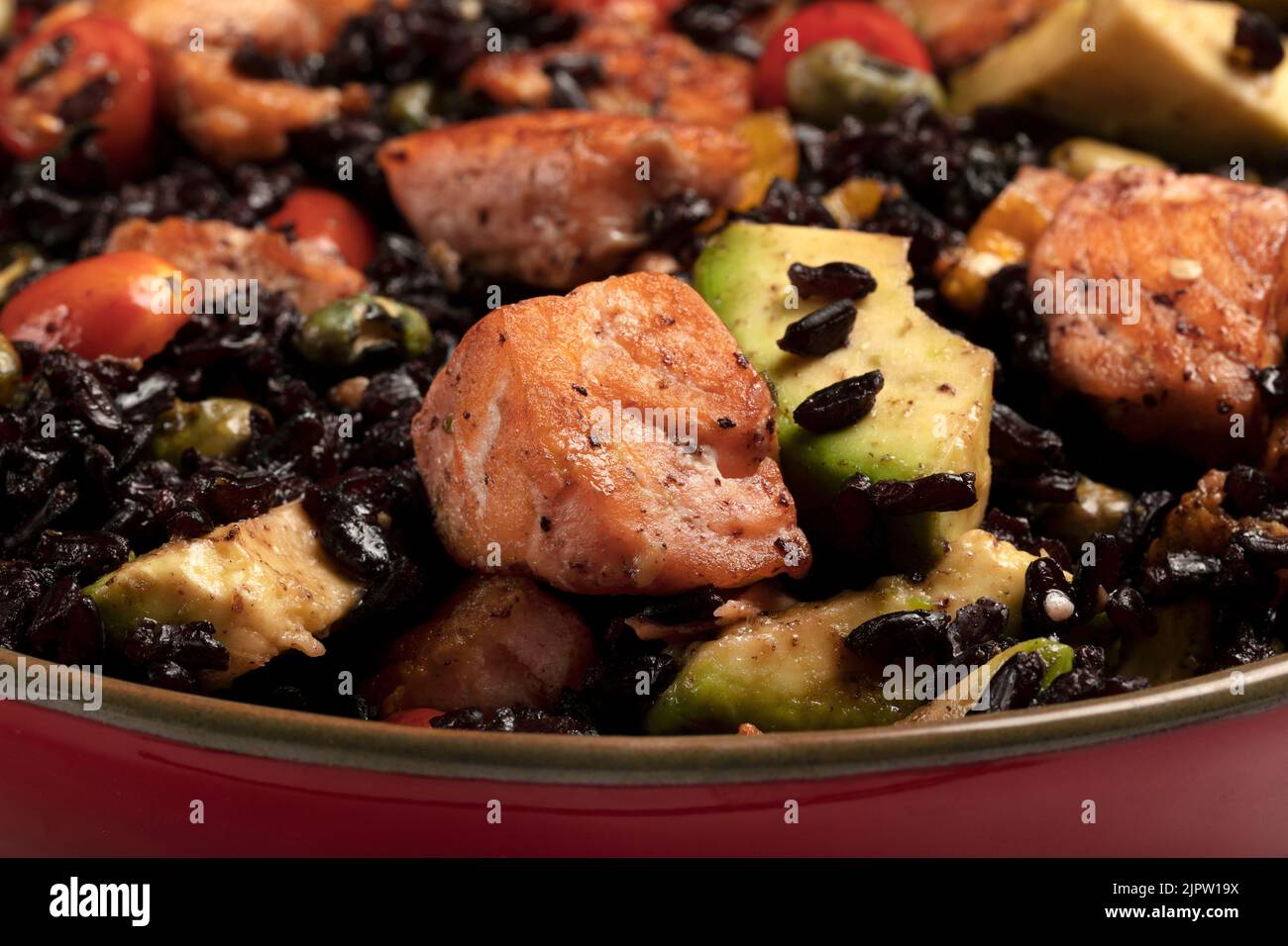 A red bowl of black rice with baked salmon, avocado, tomatoes, chili ...