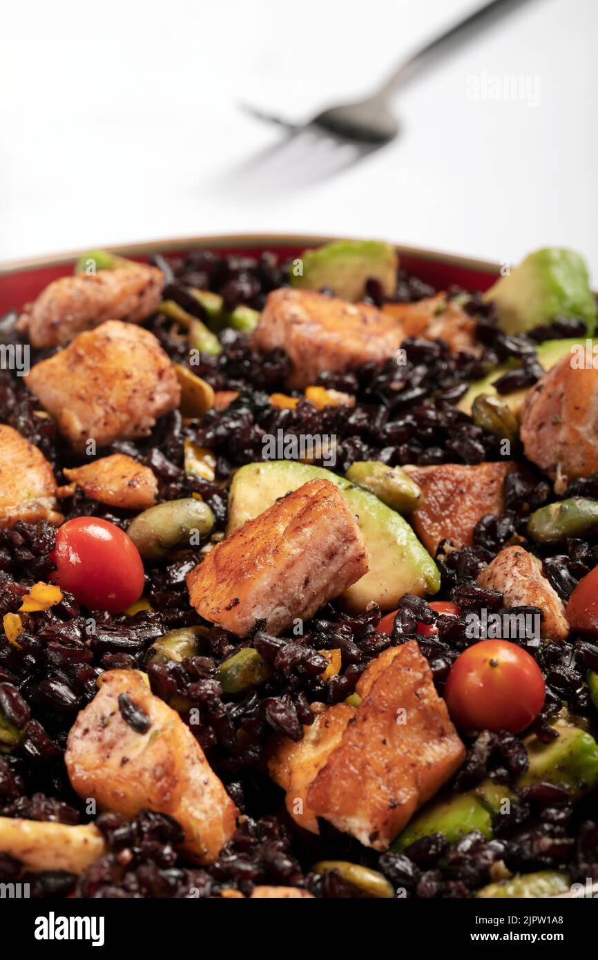 A red bowl of black rice with baked salmon, avocado, tomatoes, chili ...