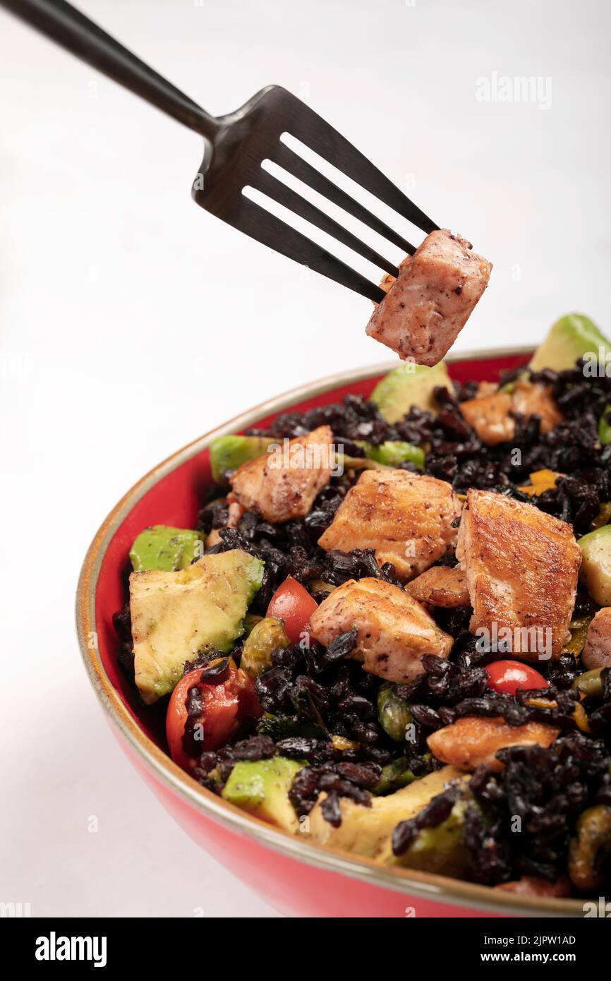 A red bowl of black rice with baked salmon, avocado, tomatoes, chili ...