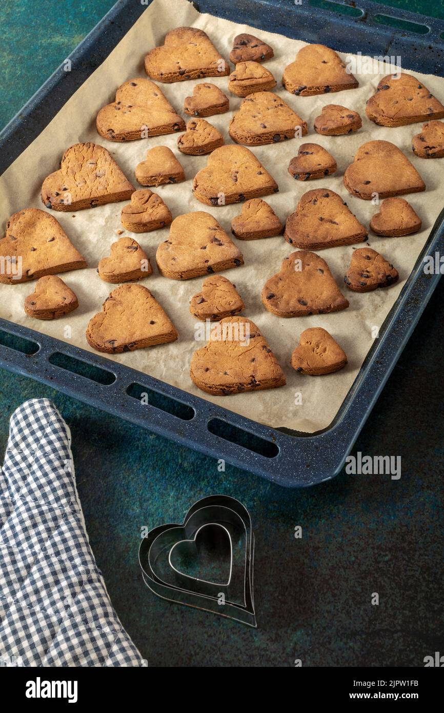 Heart shaped biscuits with chocolate drops on a baking tray near an ...