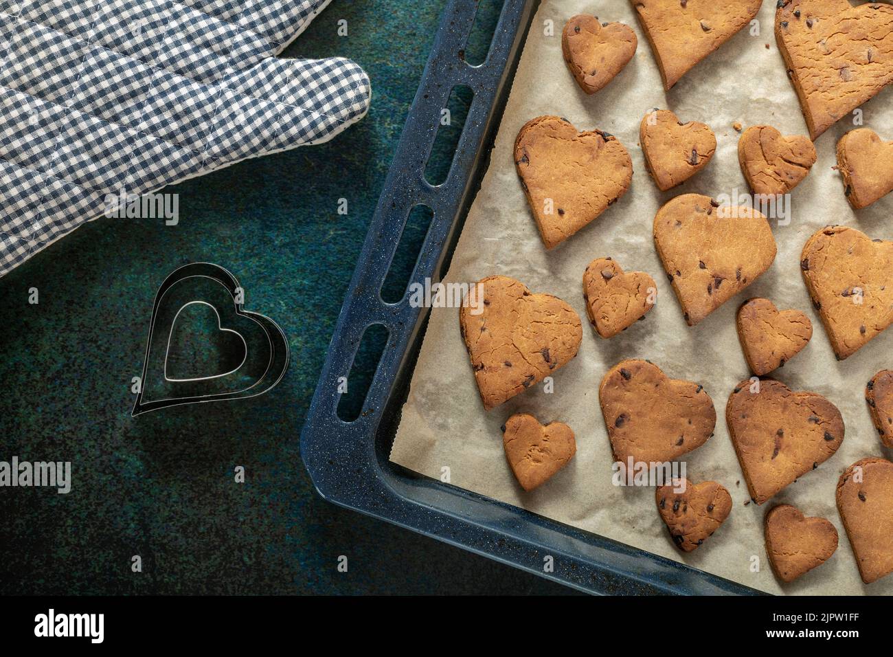 Heart shaped biscuits with chocolate drops on a baking tray near an ...