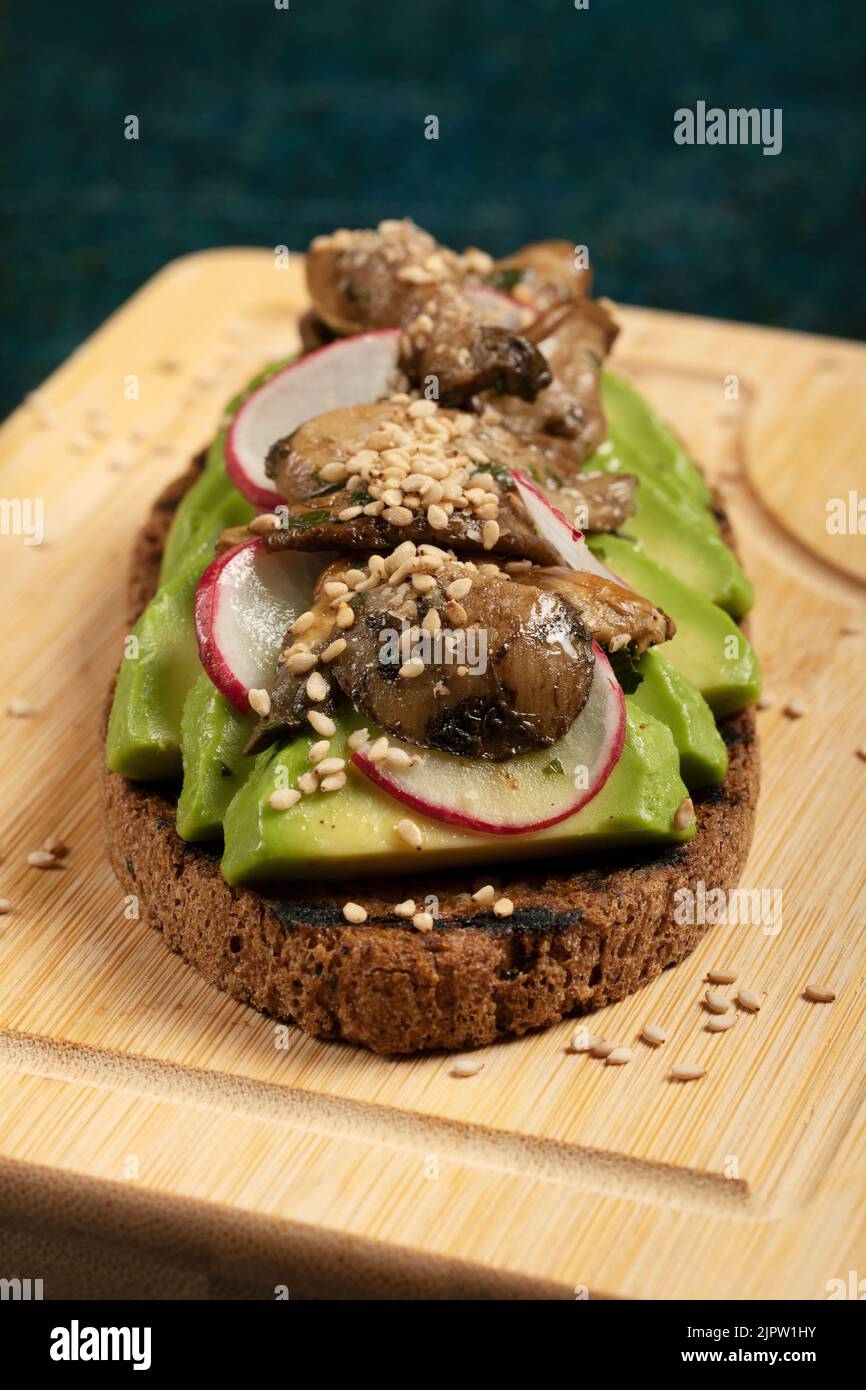 An avocado toast with mushrooms, radish and sesame seeds on a wooden ...