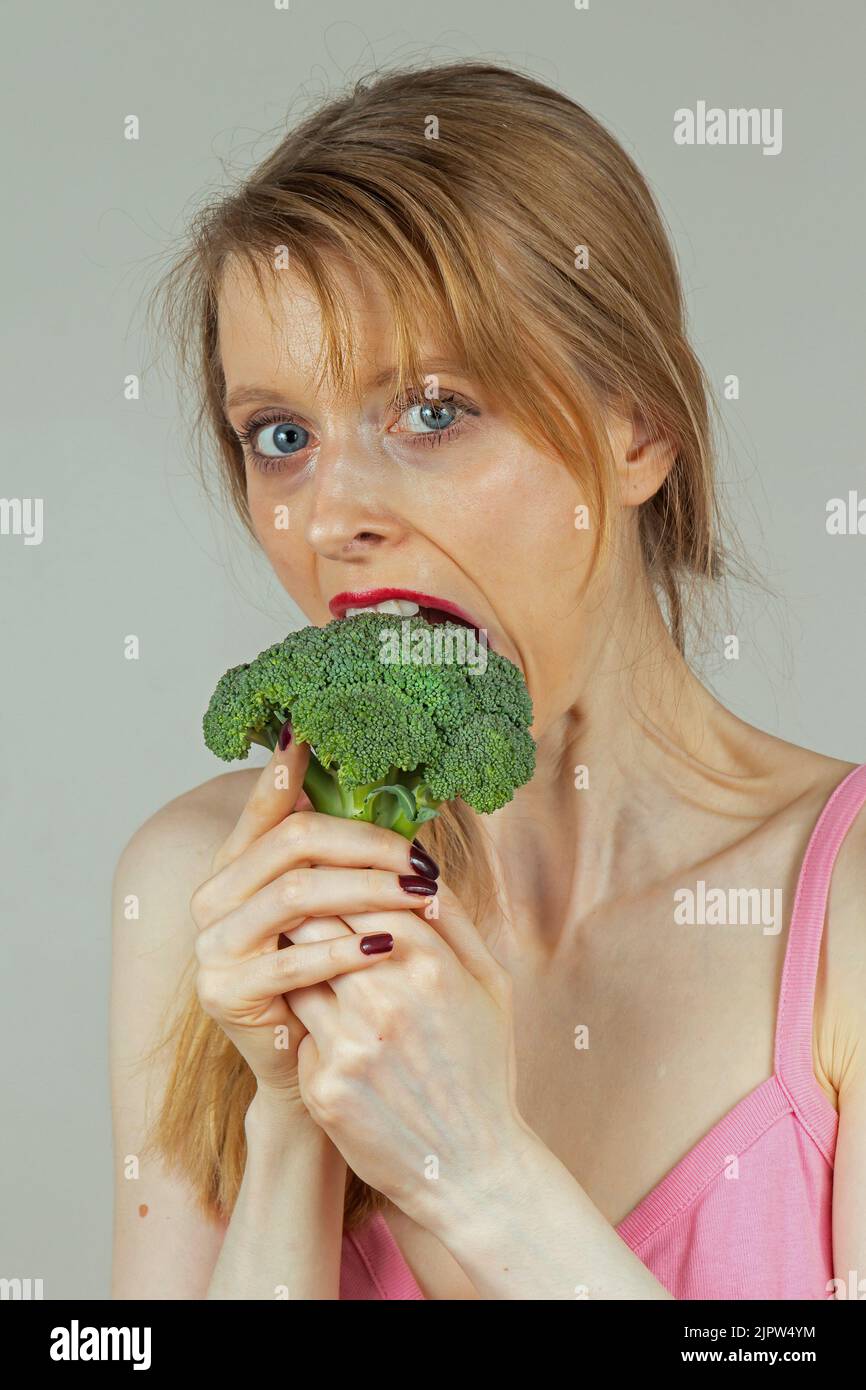 Young woman holding broccoli next to her mouth leading healthy eating ...