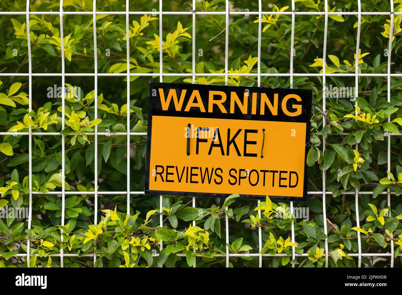 Black and yellow warning sign on a fence stating "Warning, Fake reviews ...