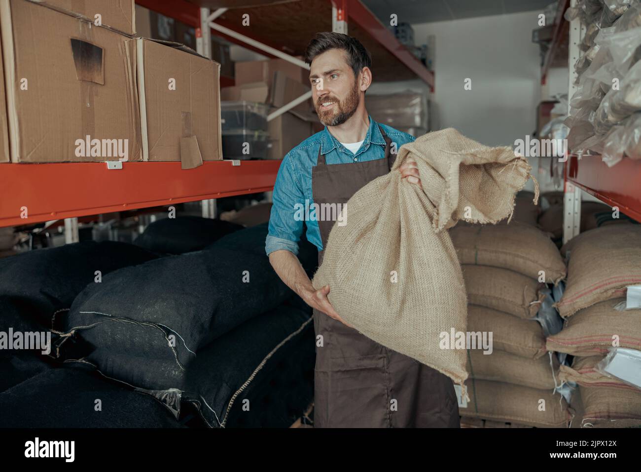 Warehouse worker with bag of fresh roasted coffee on small factory ...