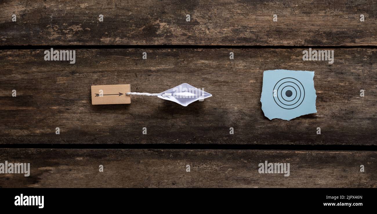 Origami boat pulling wooden peg with arrow drawn on it towards a blue ...