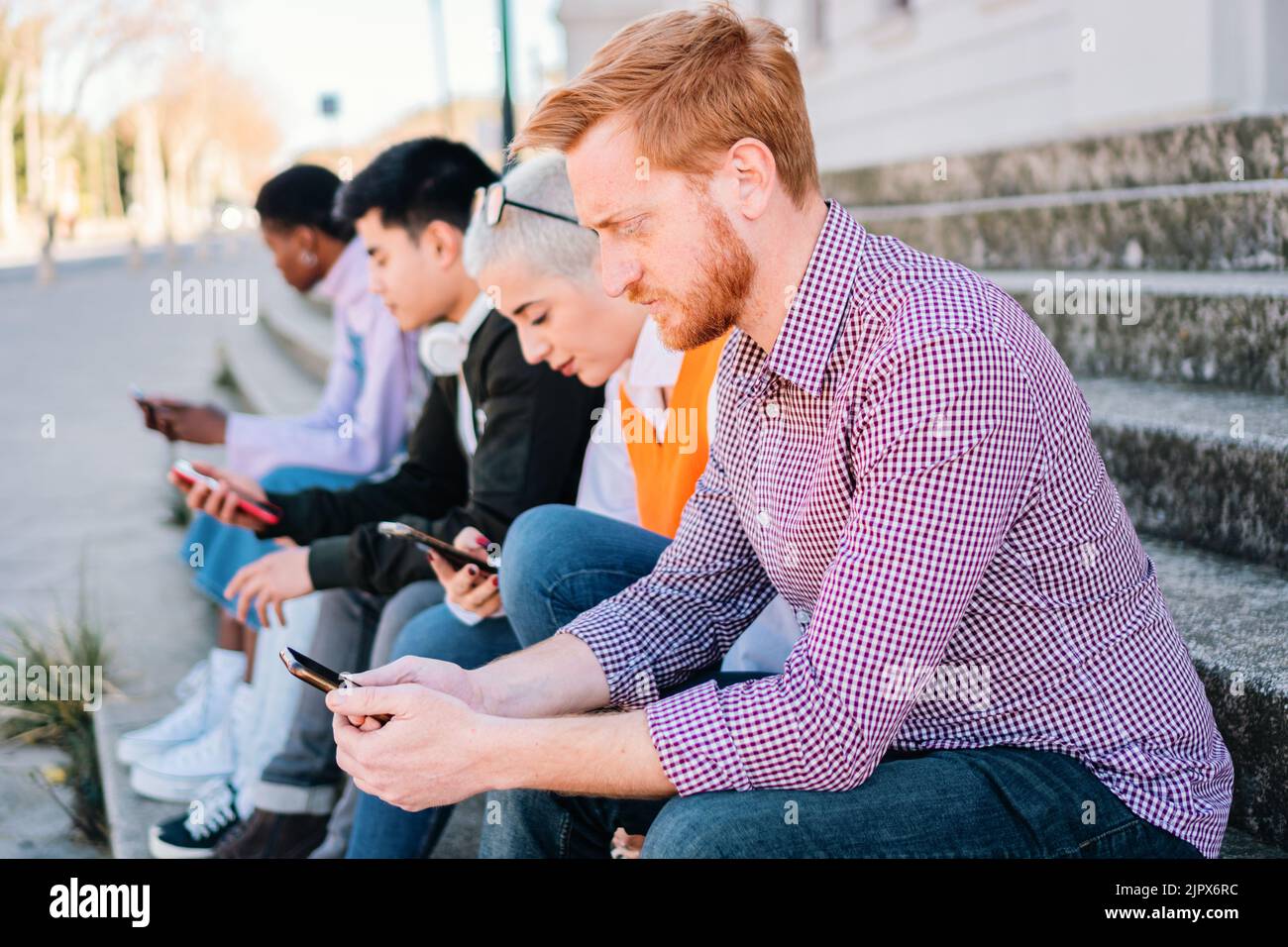Friends using smartphones and browsing on internet sitting outdoors ...