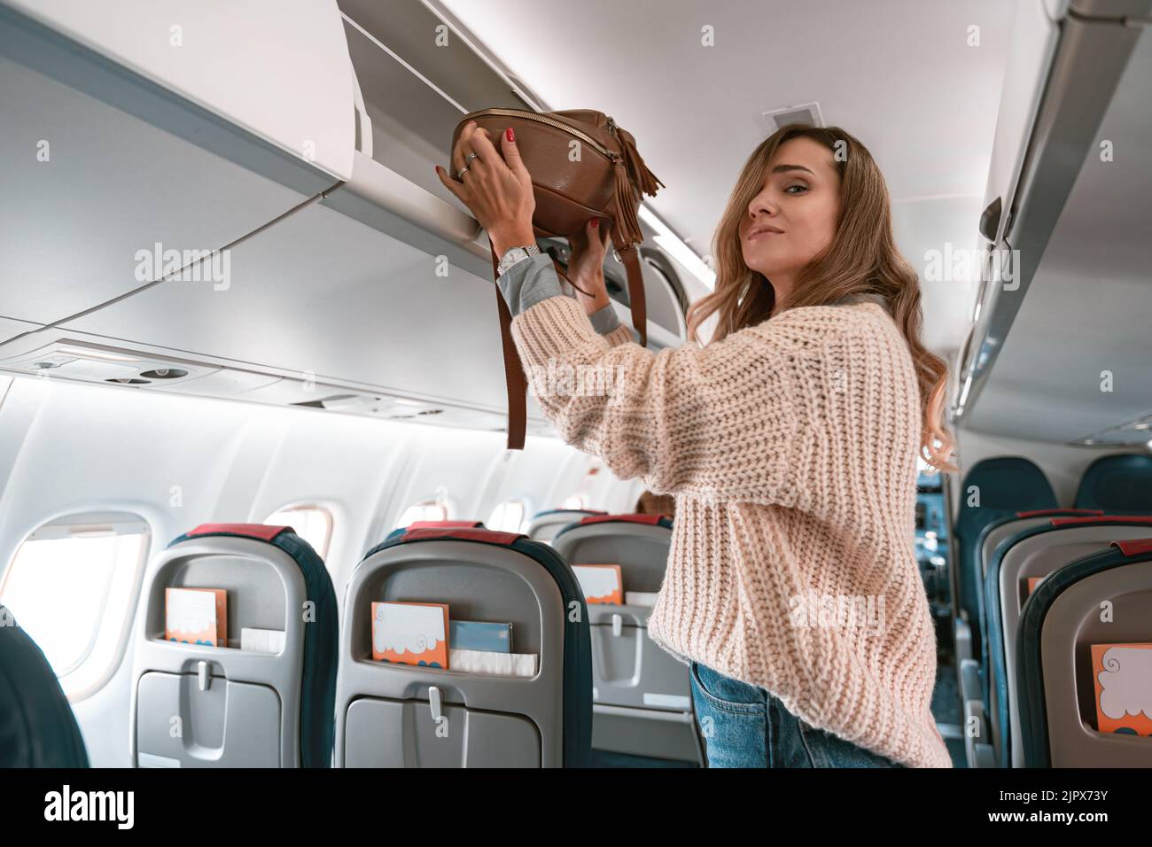 Woman traveler putting luggage into overhead locker on airplane during ...