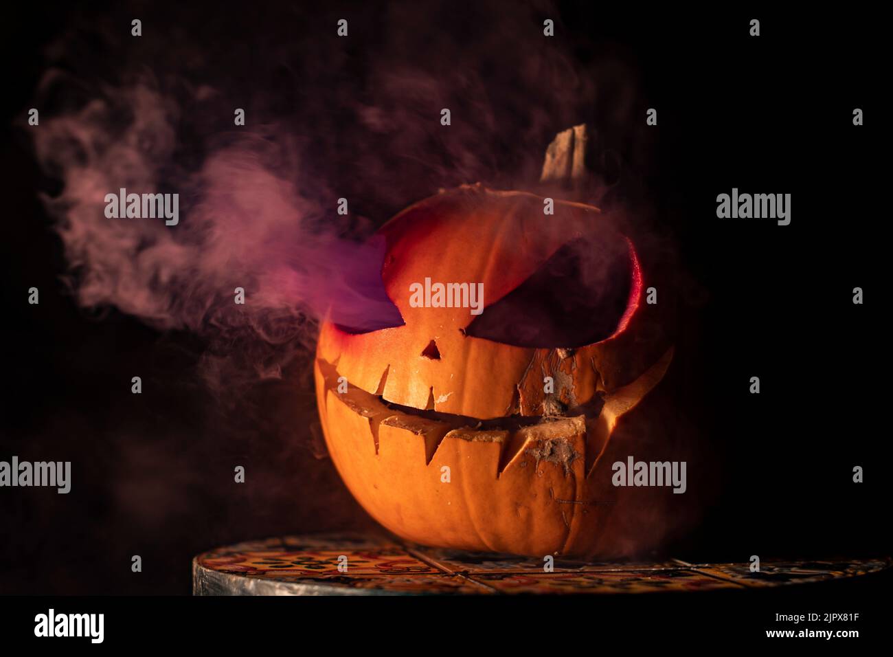 A cool shot of a Halloween carved pumpkin with purple smoke coming out ...