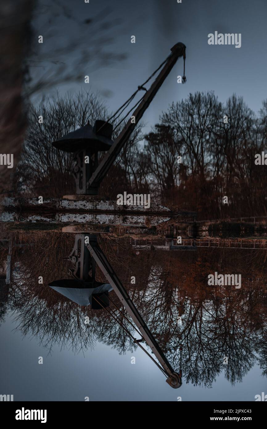 A vertical shot of an old harbor crane with reflection in water and ...