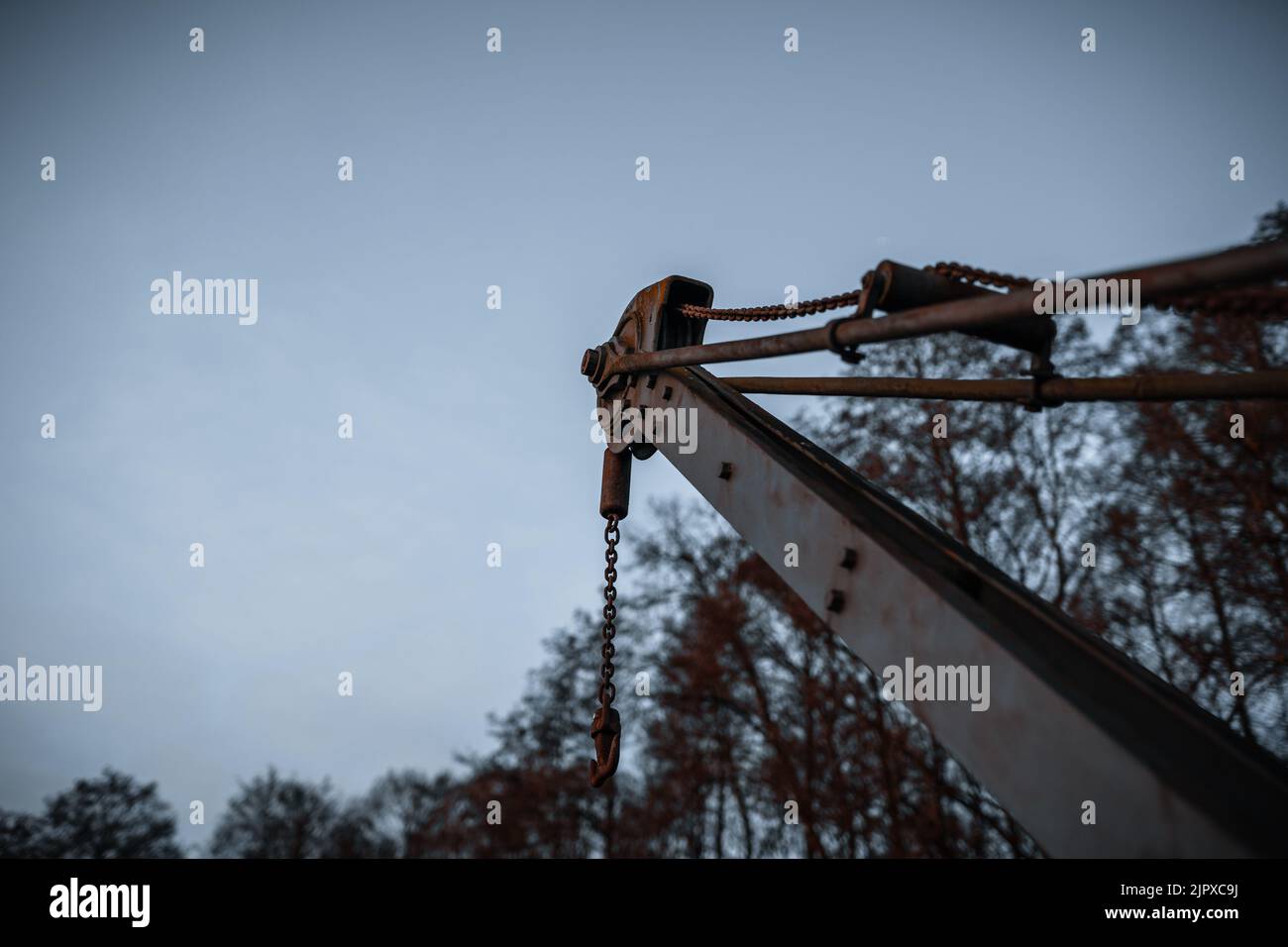 A low angle shot of an old truck crane hook against sky and trees in ...